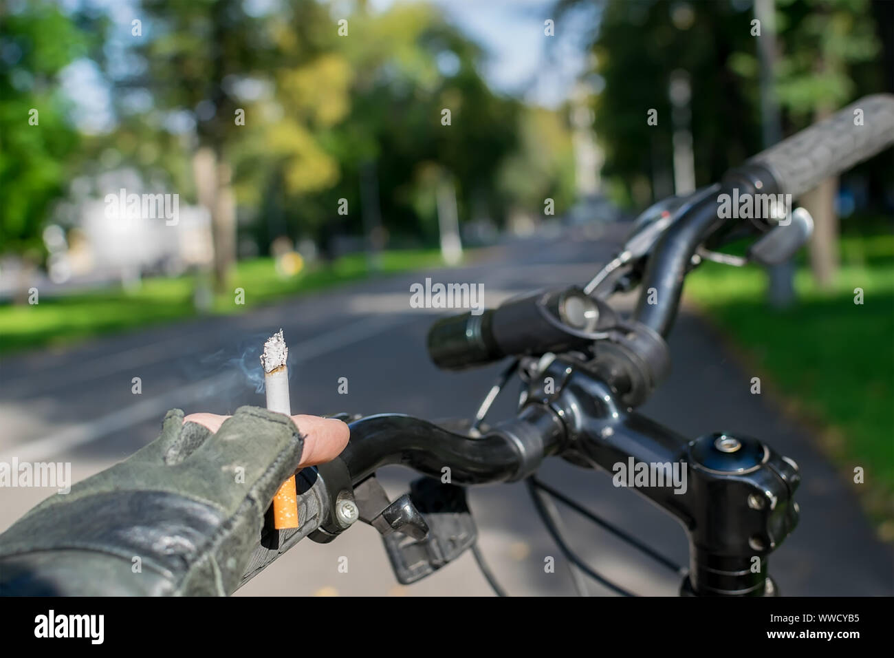cigarette in the hand of a smoking cyclist who rides a bike on the ...