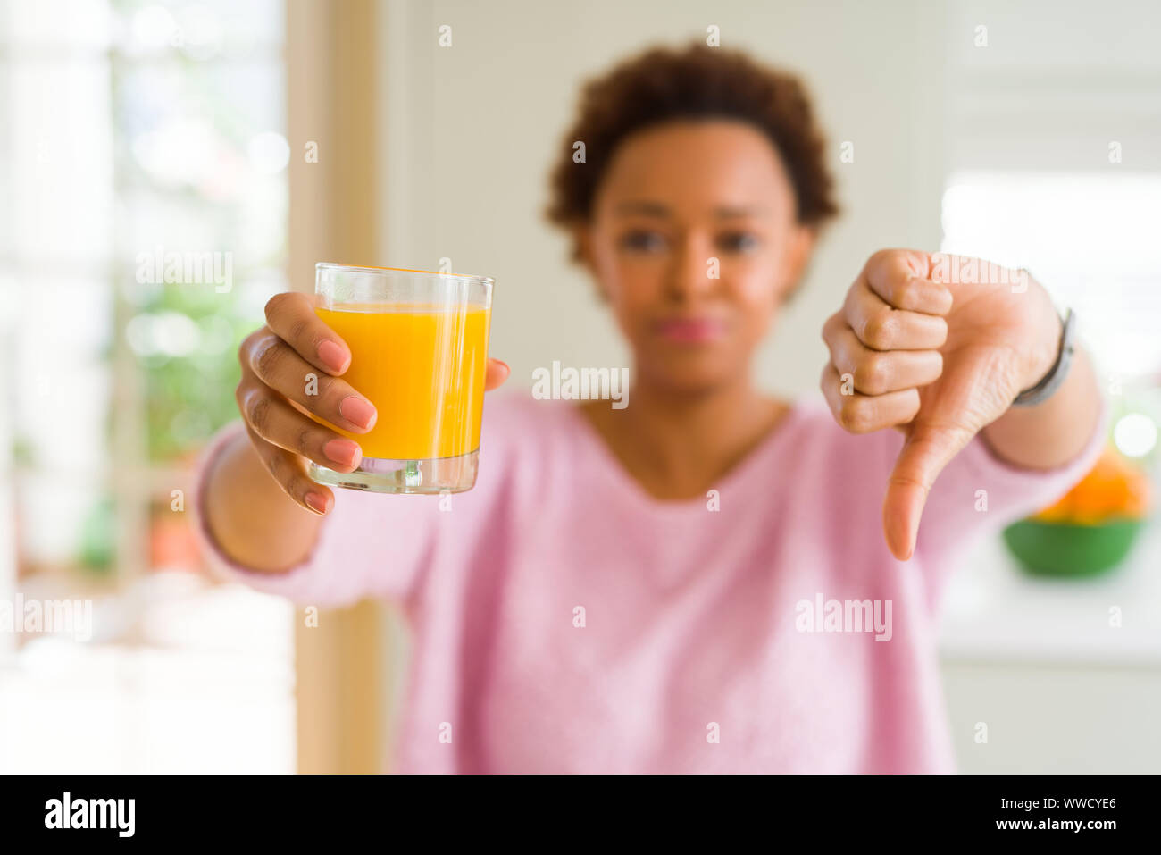 Young african american woman driking orange juice at home with angry ...