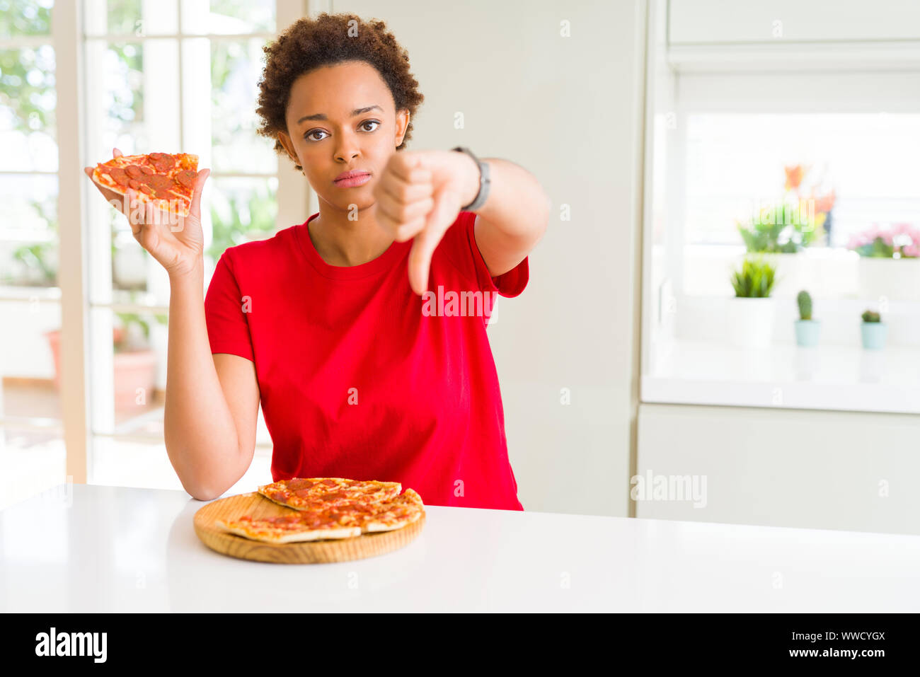 Young african american woman eating tasty peperoni pizza with angry ...