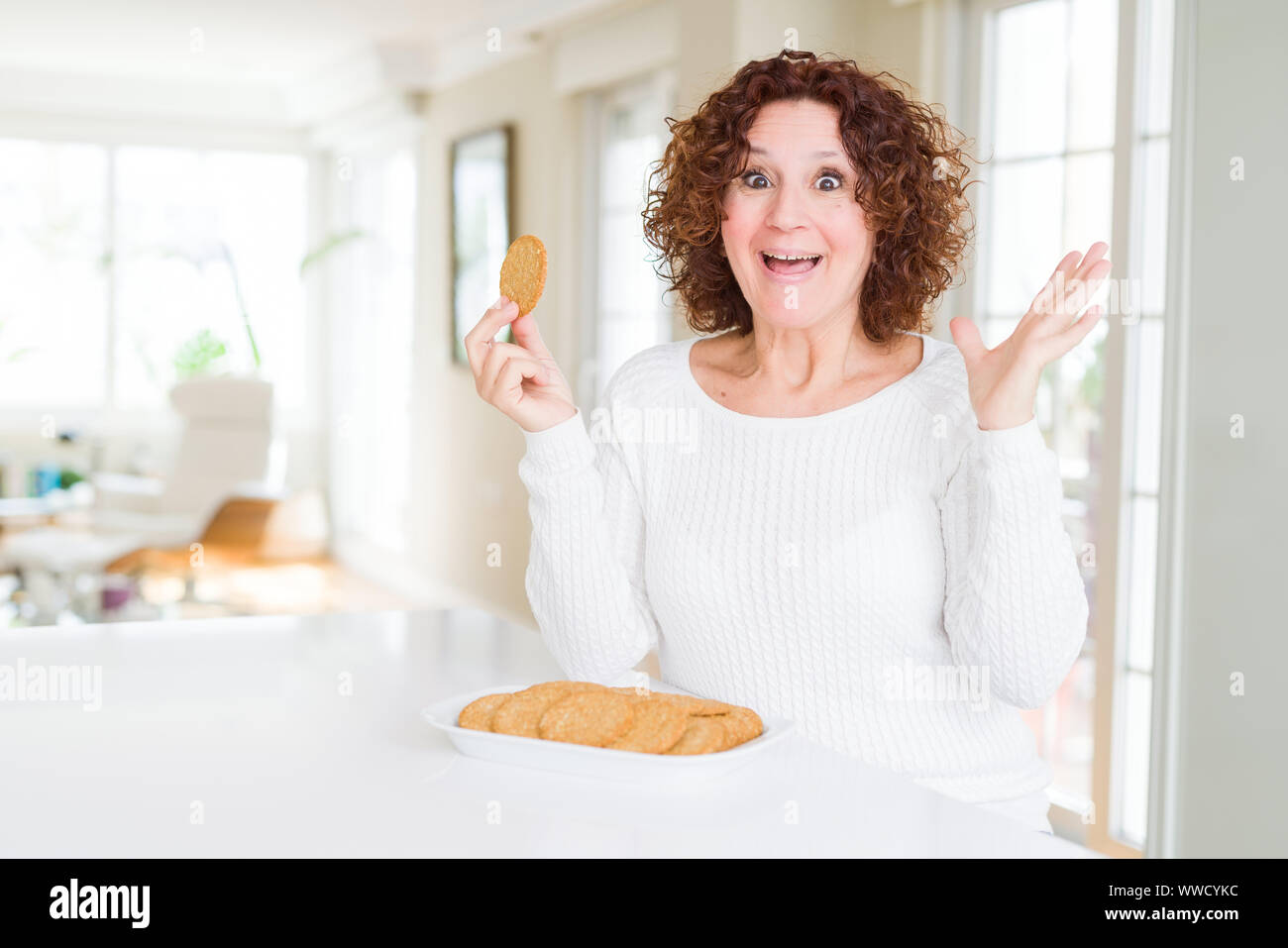 Senior woman eating healthy whole grain biscuit at home very happy and ...
