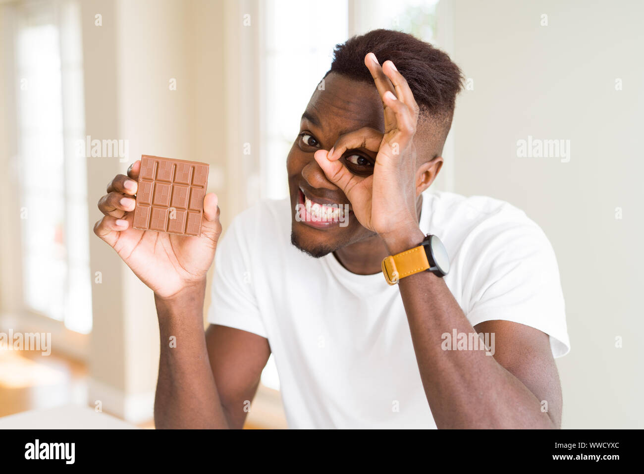 Young african american man eating chocolate bar with happy face smiling ...