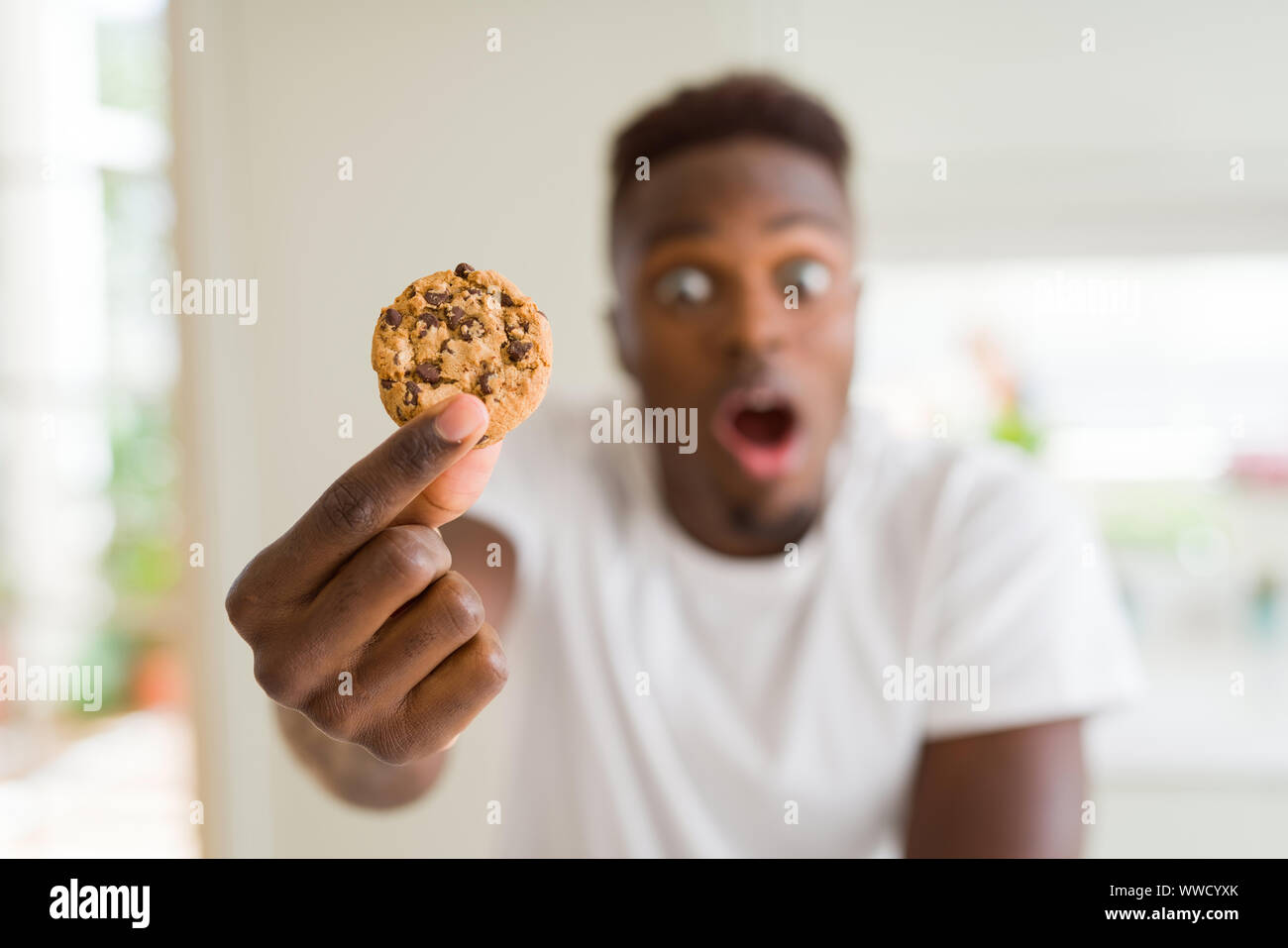 Young african american man eating chocolate chips cookies scared in ...