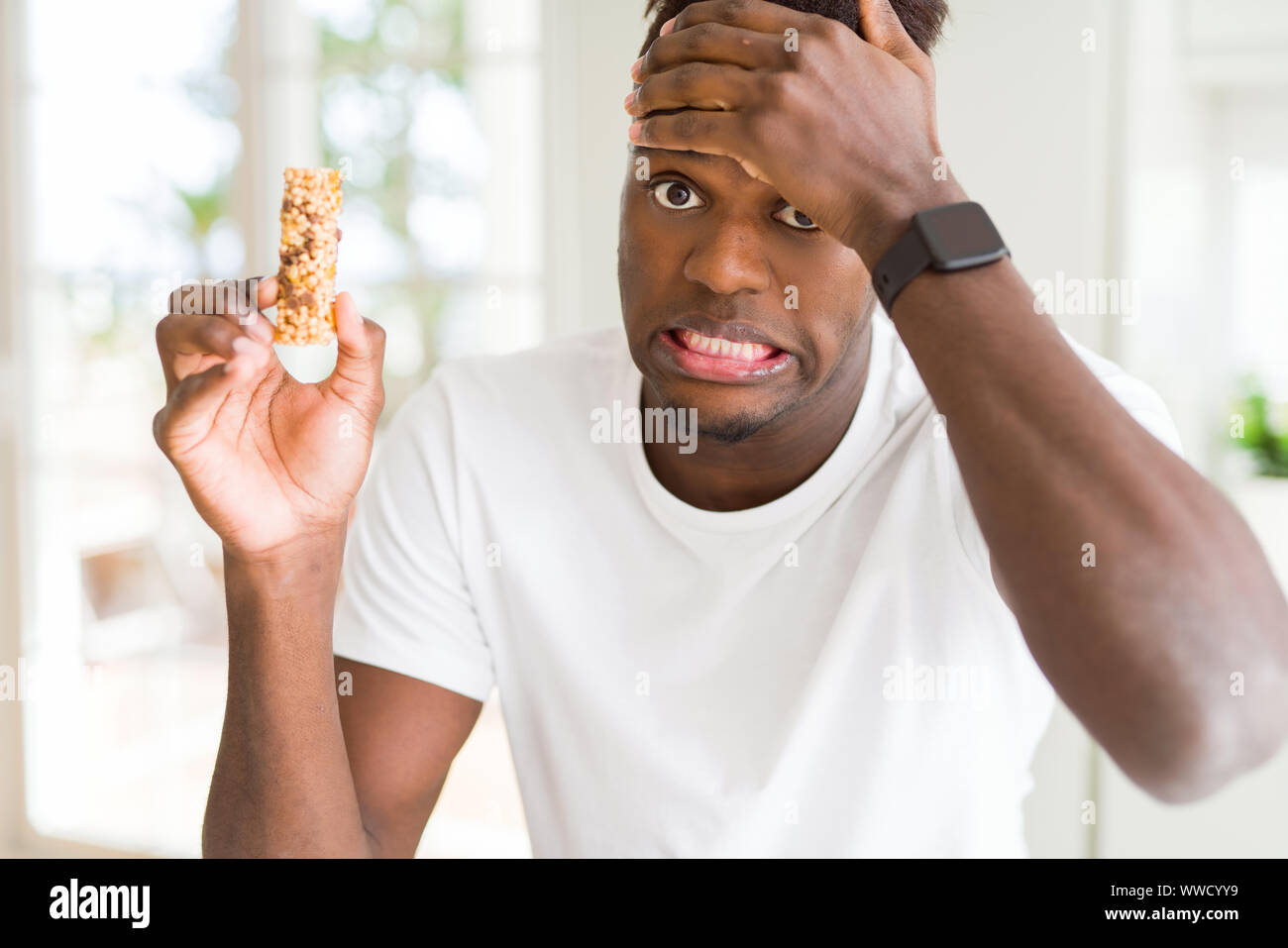 African american man eating energetic cereals bar stressed with hand on ...