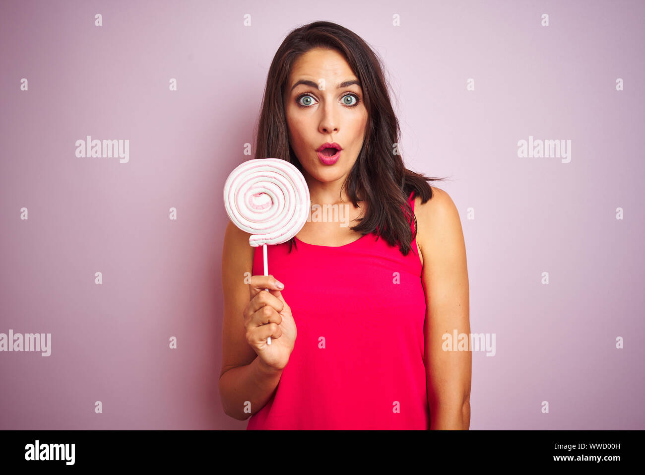 Young beautiful woman eating sweet candy over pink isolated background ...