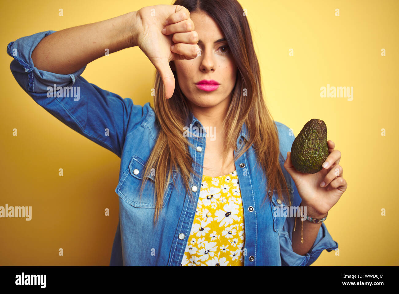 Young beautiful woman eating healthy avocado over yellow background ...