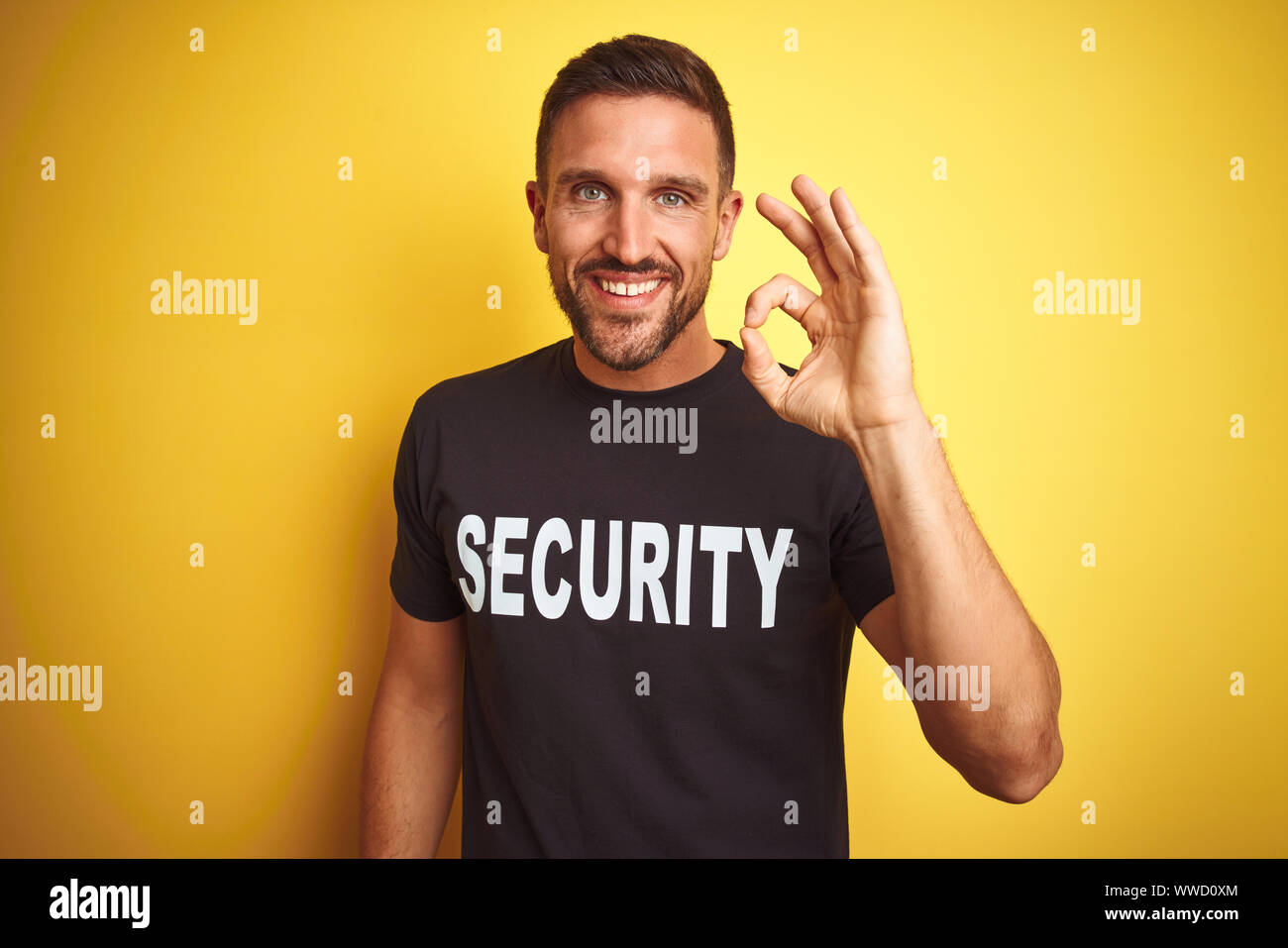 Young safeguard man wearing security uniform over yellow isolated ...