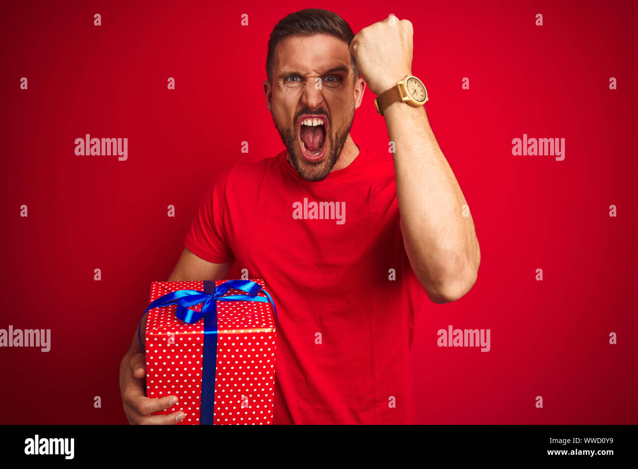 Young man holding birthday present over isolated red background annoyed ...