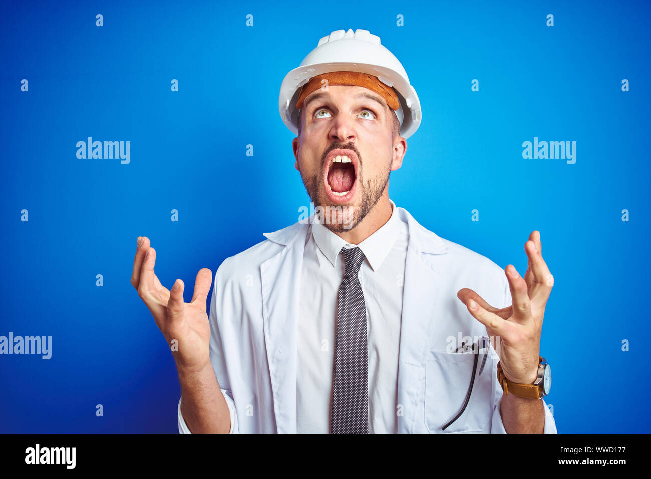 Young handsome engineer man wearing safety helmet over blue isolated ...