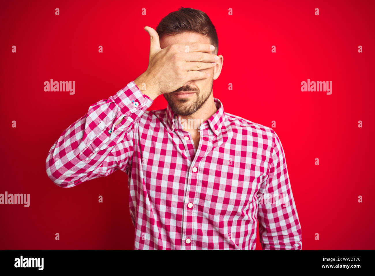 Young handsome man over red isolated background covering eyes with hand ...