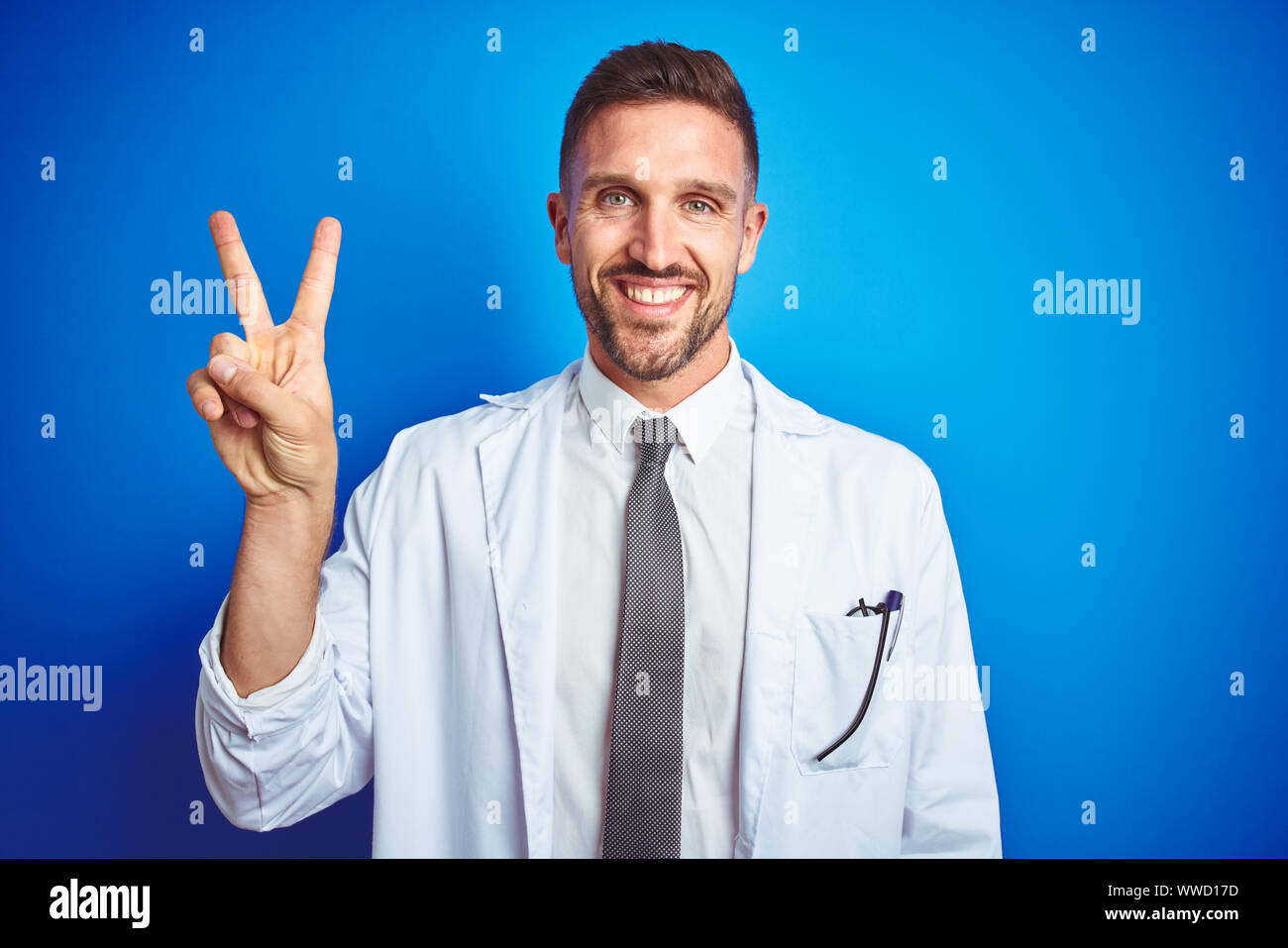Young handsome doctor man wearing white professional coat over isolated ...