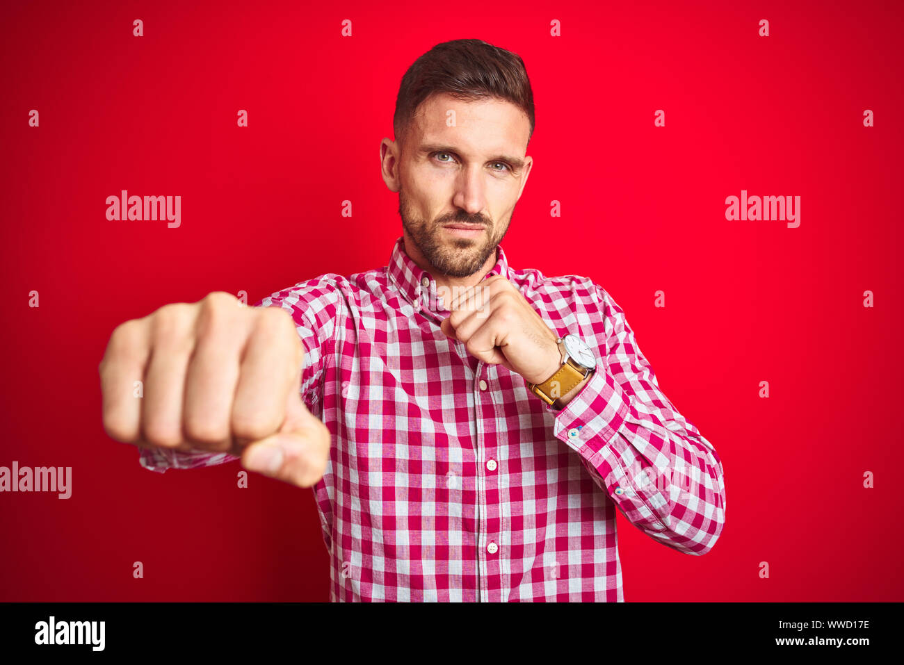 Young handsome man over red isolated background Punching fist to fight ...