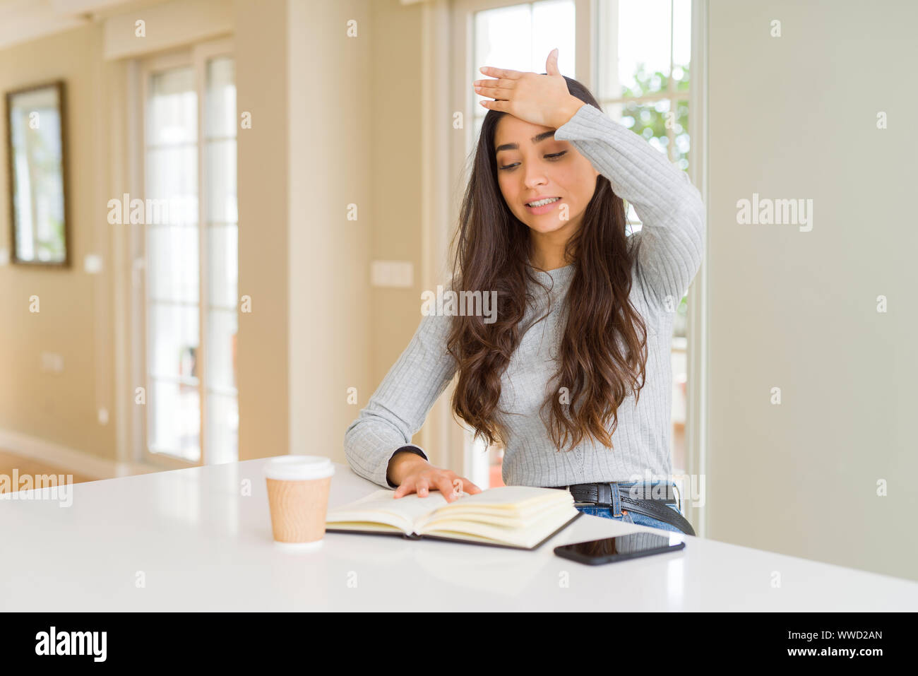 Young woman reading a book and drinking a coffe stressed with hand on ...