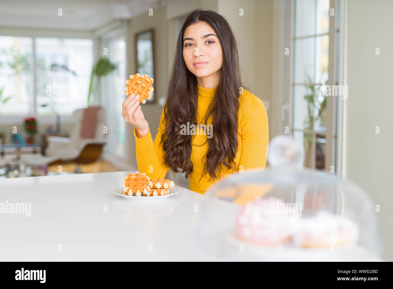 Young woman eating sweet waffle pastry with a confident expression on ...