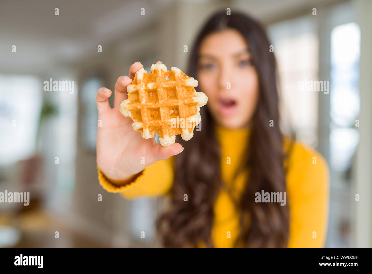 Young woman eating sweet waffle pastry scared in shock with a surprise ...