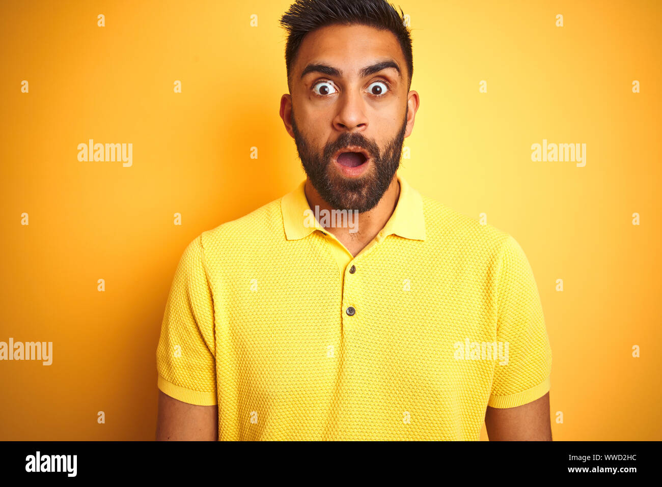 Young indian man wearing polo standing over isolated yellow background ...