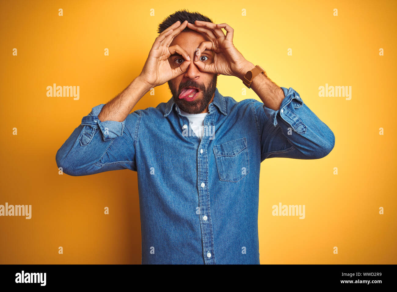 Young indian man wearing denim shirt standing over isolated yellow ...