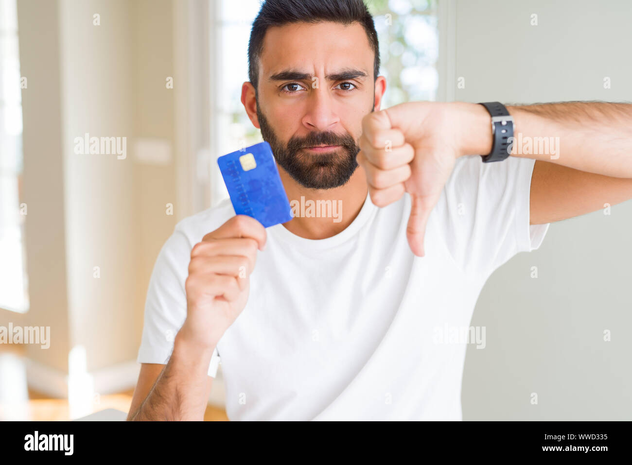 Handsome hispanic man holding credit card with angry face, negative ...