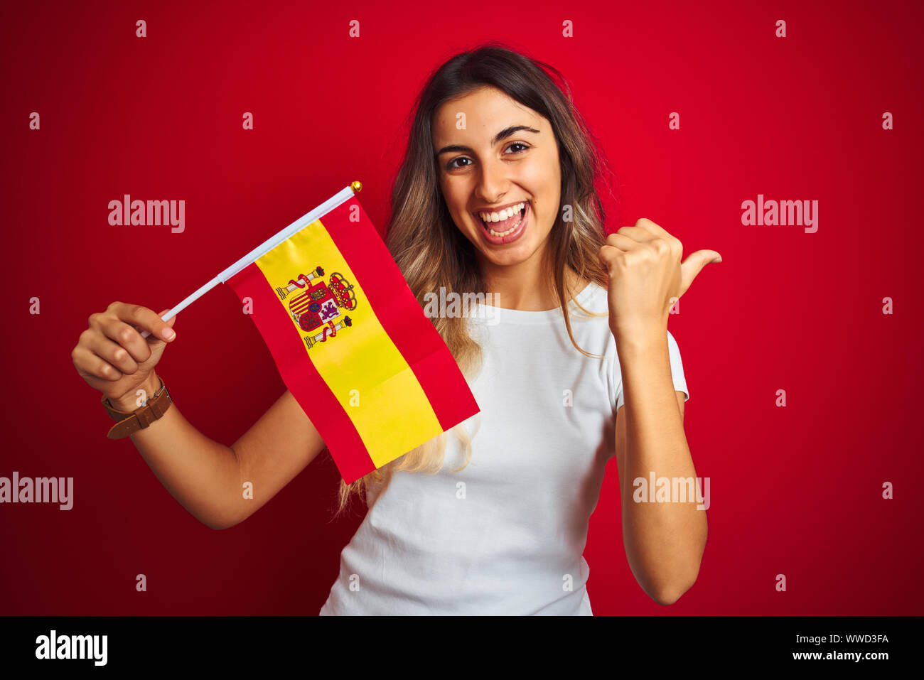 Young beautiful woman holding spanish flag over red isolated background ...