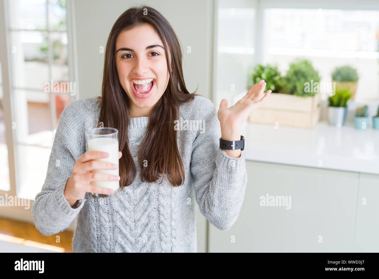 Beautiful young woman drinking a glass of fresh milk very happy and ...