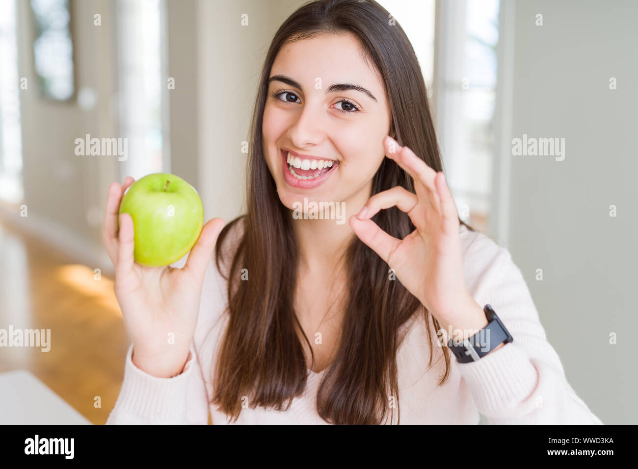 Beautiful young woman eating healthy green apple fruit doing ok sign ...