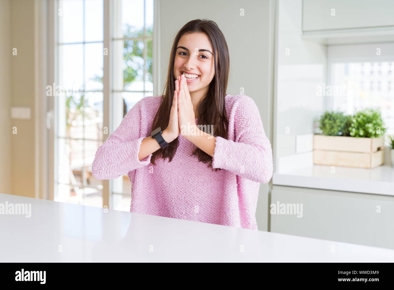 Beautiful young woman wearing pink sweater praying with hands together ...