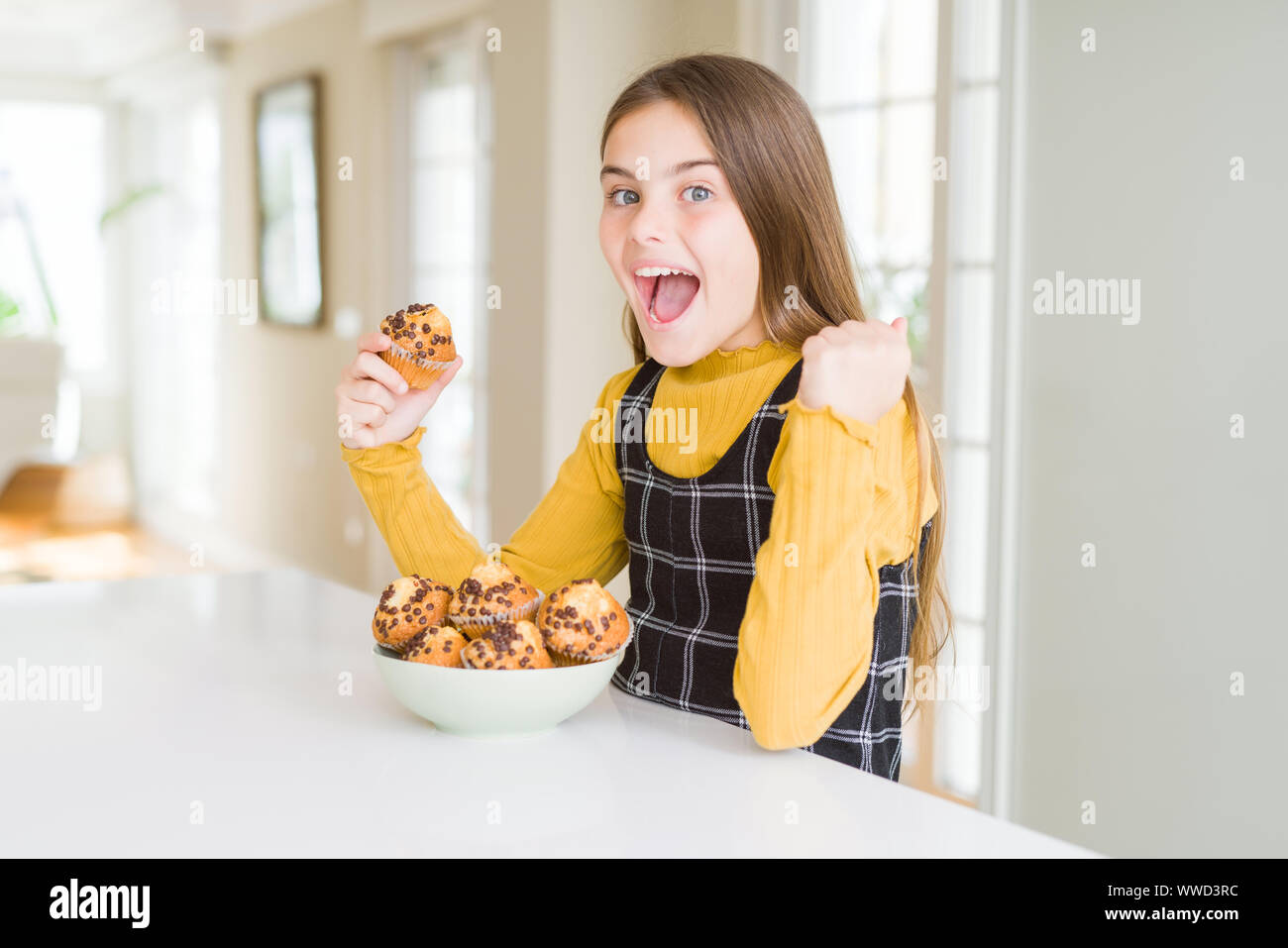Beautiful young girl eating chocolate chips muffins screaming proud and ...
