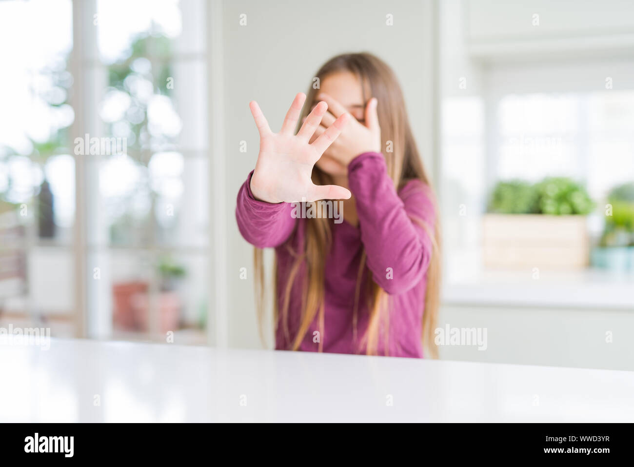 Beautiful young girl kid on white table covering eyes with hands and ...