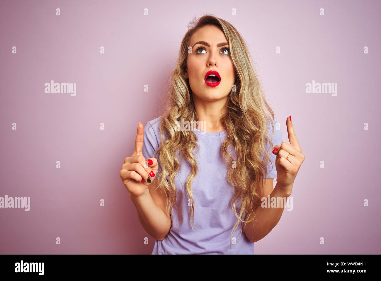 Young beautiful woman wearing purple t-shirt standing over pink ...