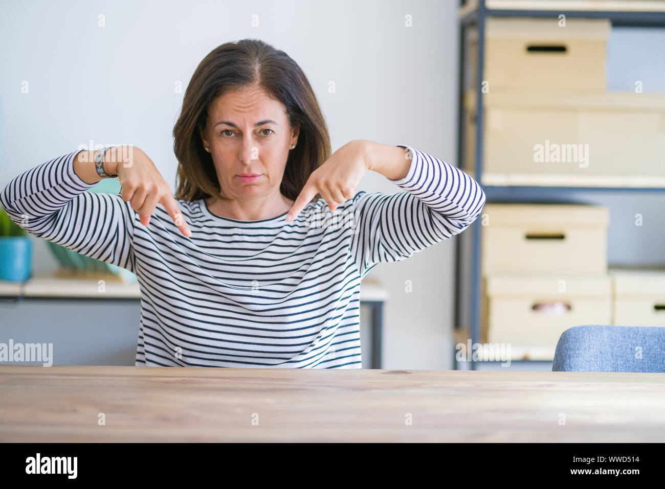 Middle age senior woman sitting at the table at home Pointing down ...