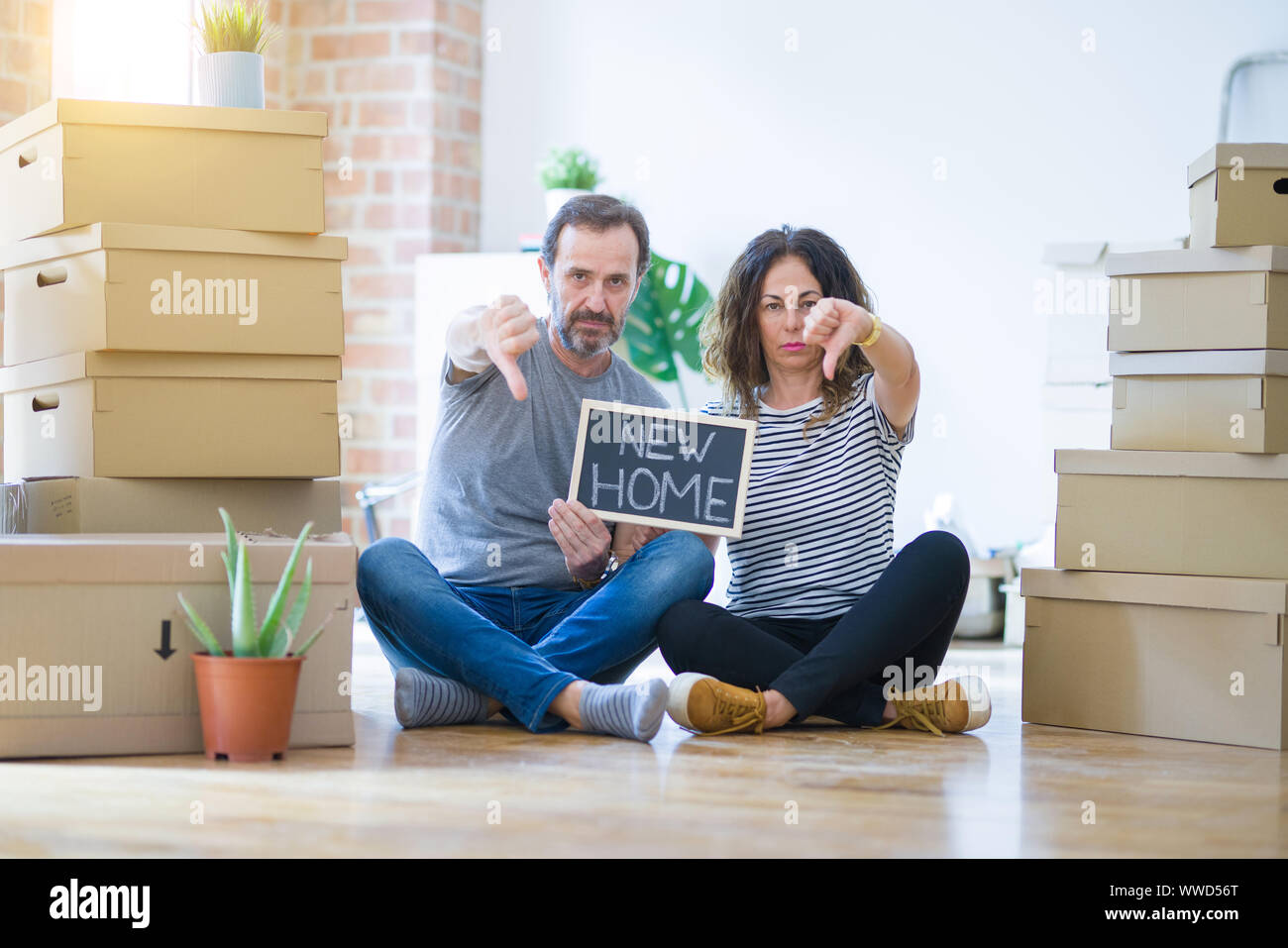 Middle age senior couple sitting on the floor holding blackboard moving ...