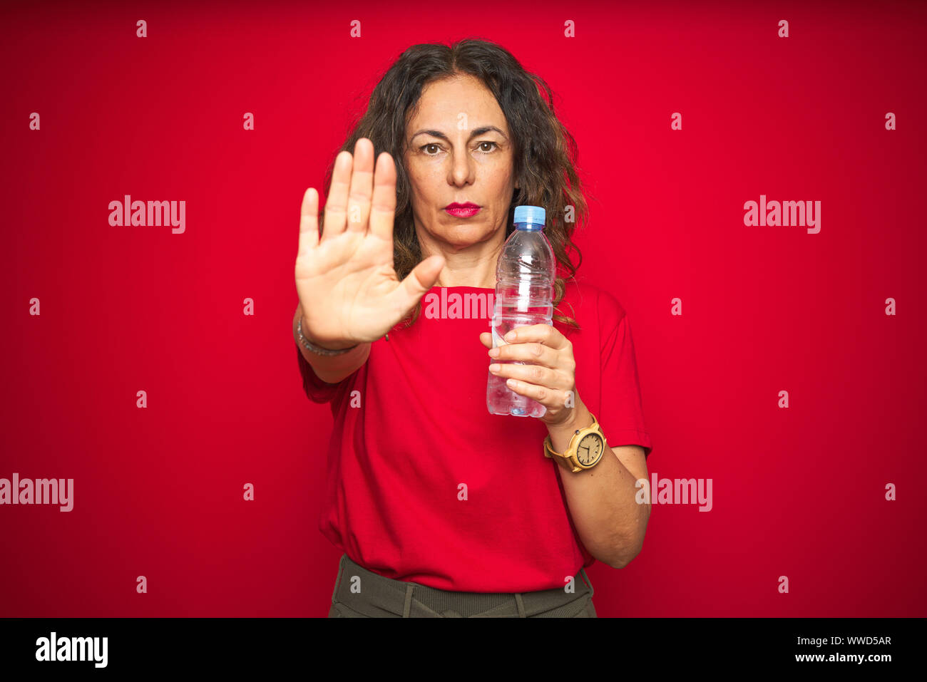 Middle age senior woman holding plastic water bottle over red isolated ...
