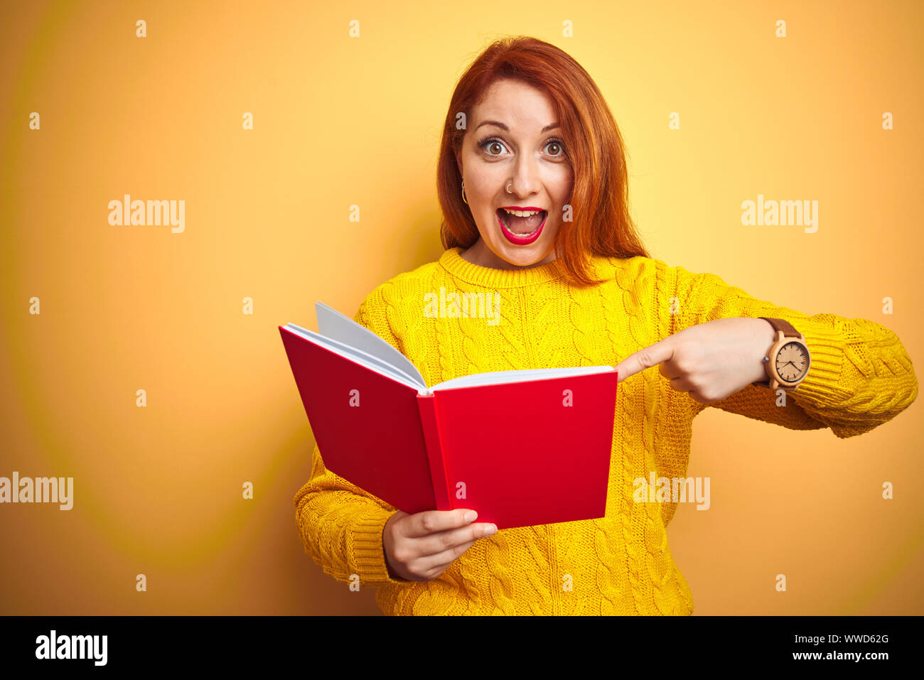 Young redhead teacher woman reading red book over yellow isolated ...