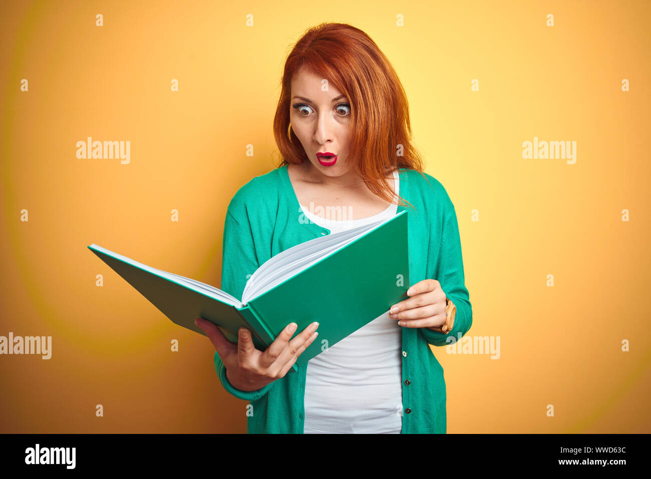 Young redhead student woman reading green book over yellow isolated ...