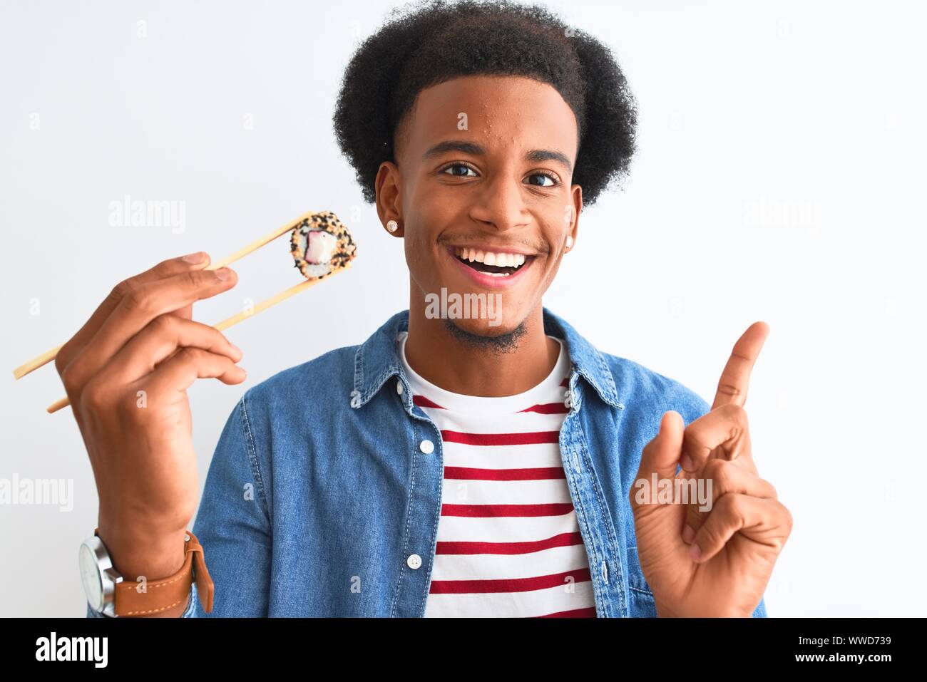 Young african american man eating sushi using chopsticks over isolated ...