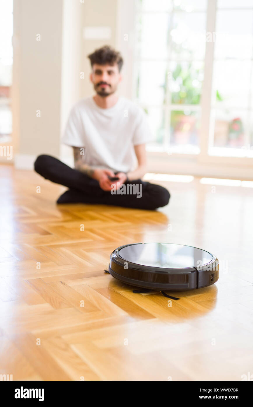 Young man using automatic vacuum cleaner to clean the floor, controling ...