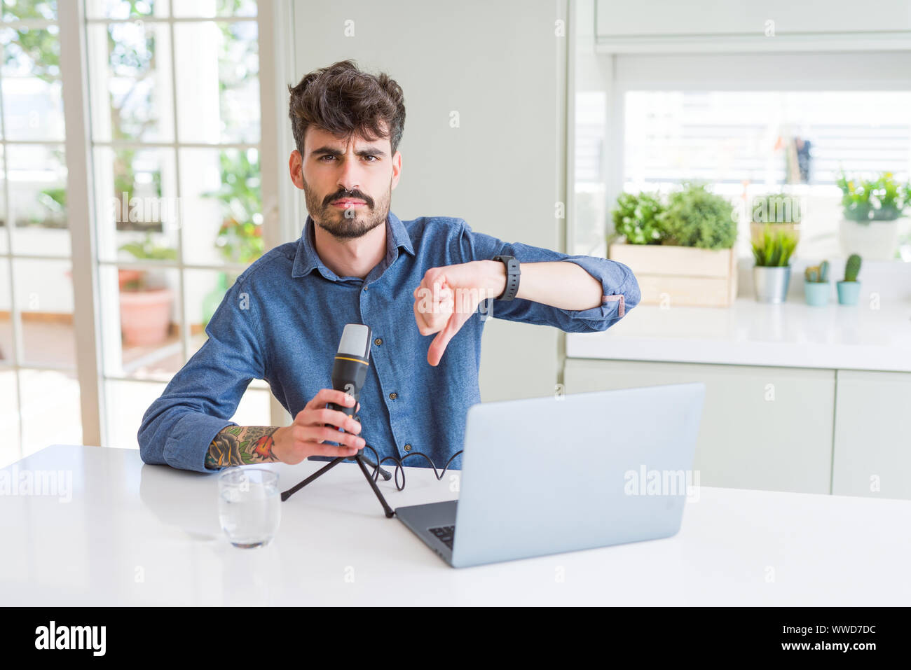 Young man recording podcast using microphone and laptop with angry face ...