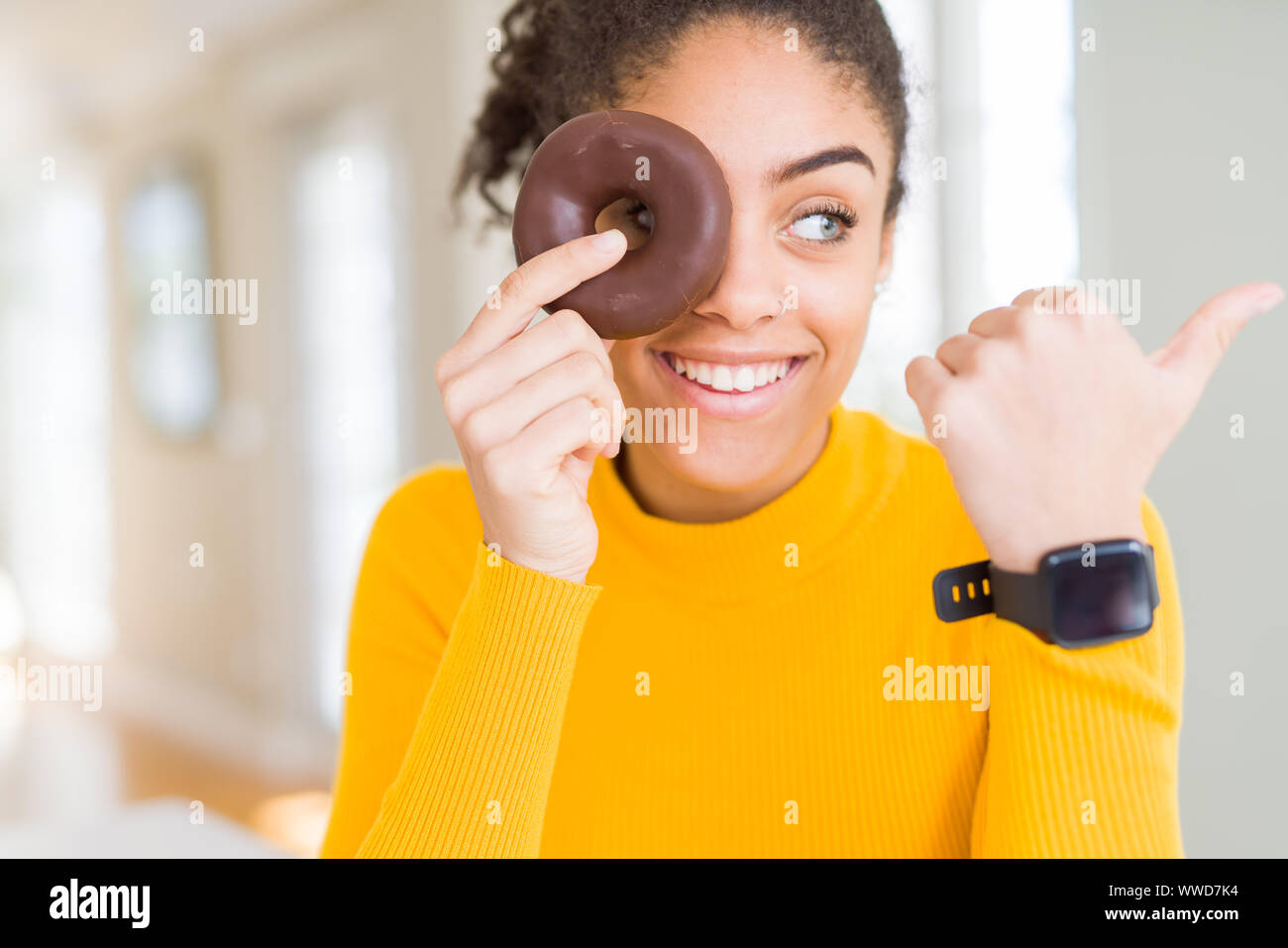 Young african american girl eating sweet chocolate donut pointing and ...
