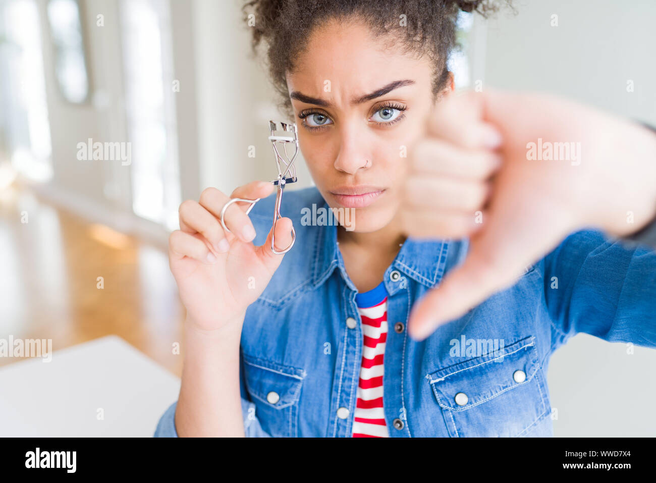 Young african american girl using eyelashes curler with angry face ...