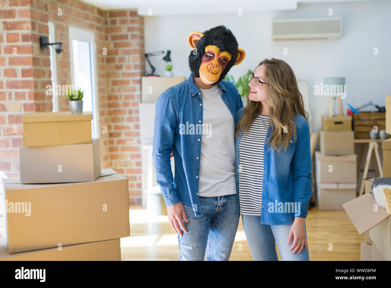 Young couple having fun wearing a monkey mask moving to a new apartment ...