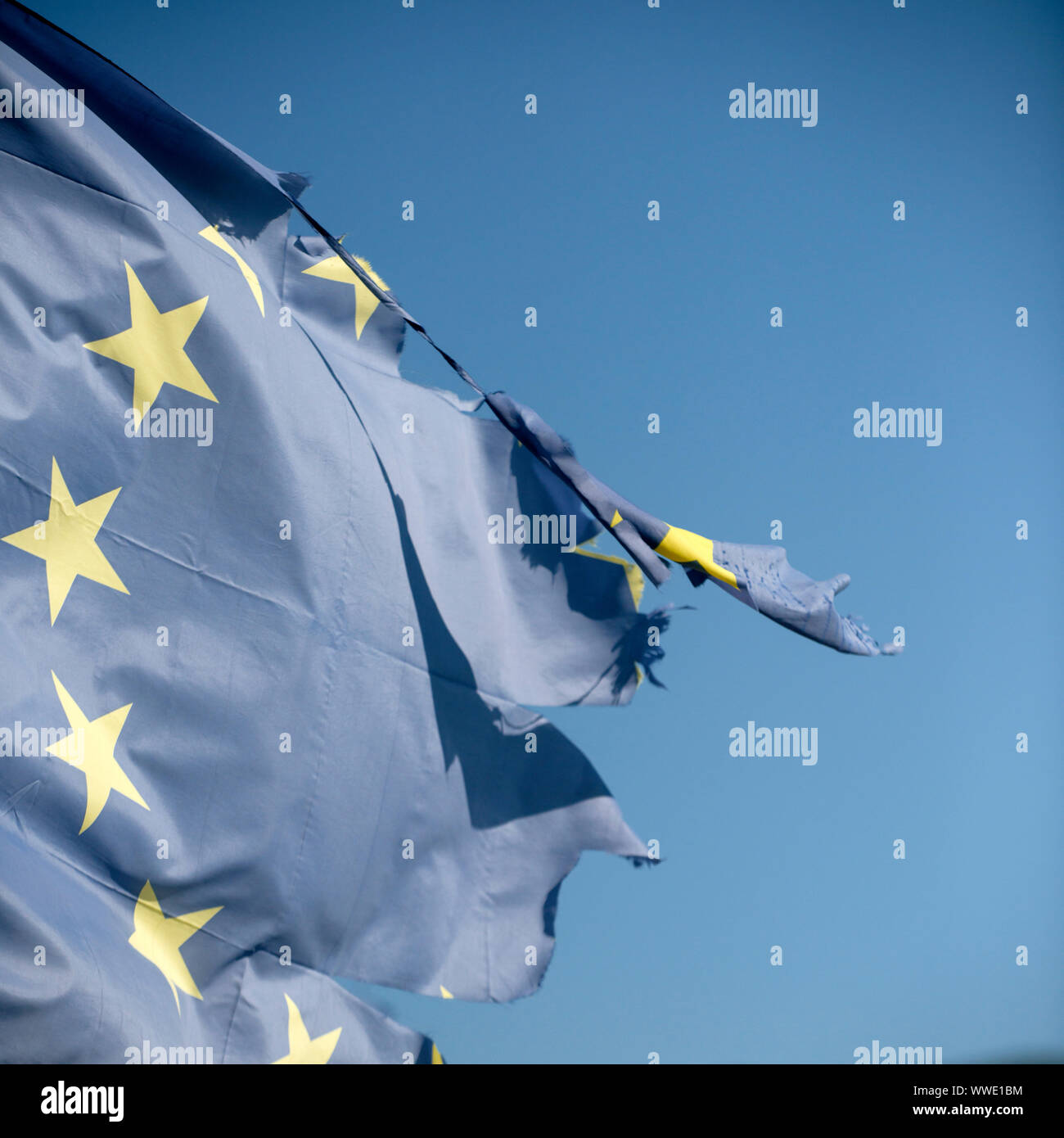 European union twelve star flag torn and with knots in wind on blue sky ...