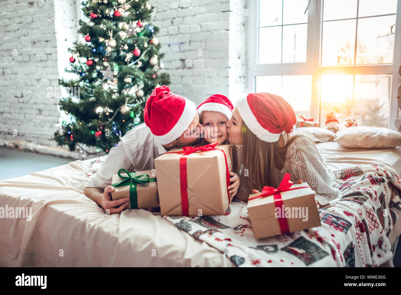 Happy parents kissing daughter and giving xmas present on bed ... Happy parents kissing daughter and giving xmas present on bed ...