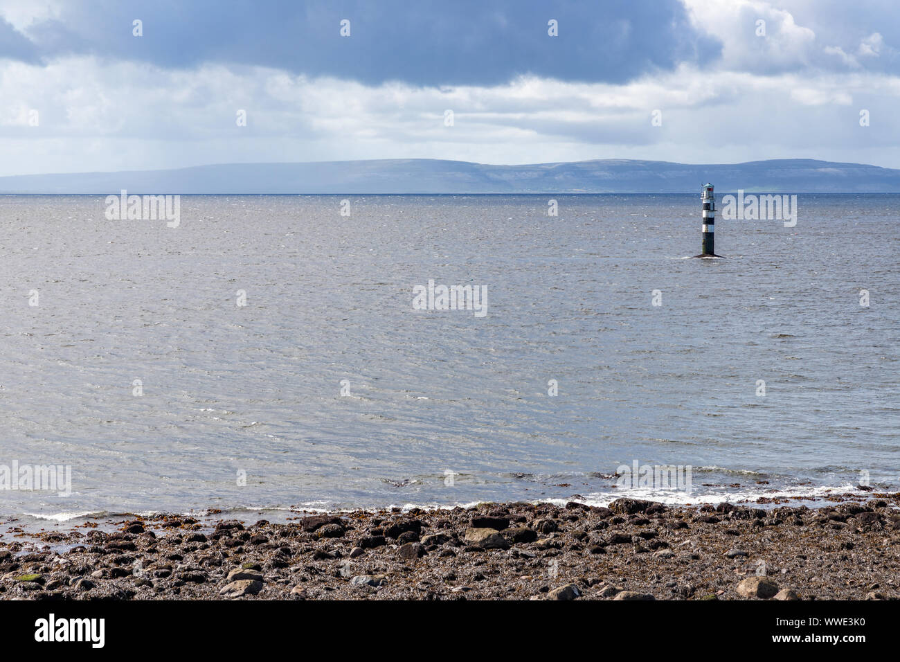 Lighthouse in Galway bay with rainy cloud and burren mountains in ...
