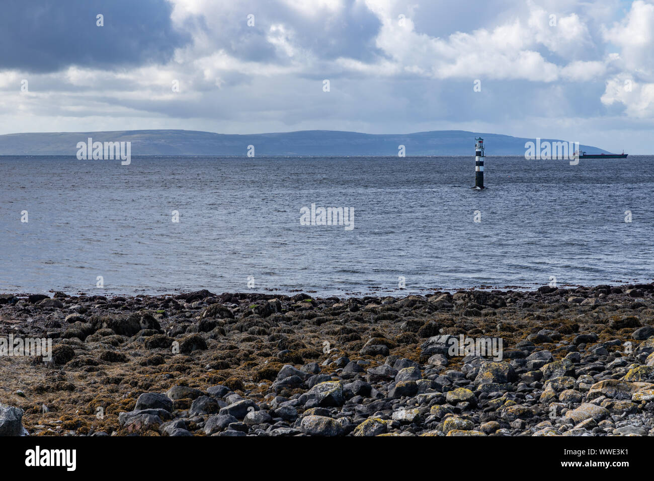 Lighthouse in Galway bay with rainy cloud and burren mountains in ...