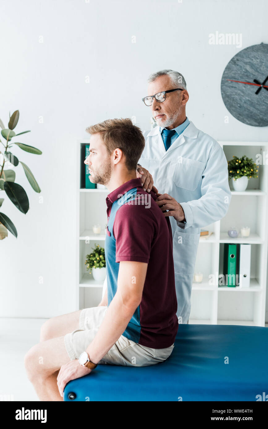 chiropractor in white coat and glasses touching back of handsome ...