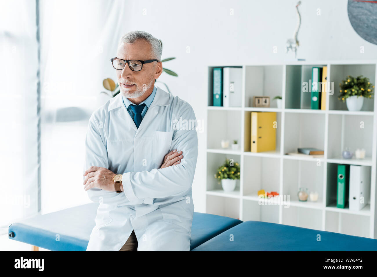bearded doctor in glasses and white coat sitting on massage table with ...