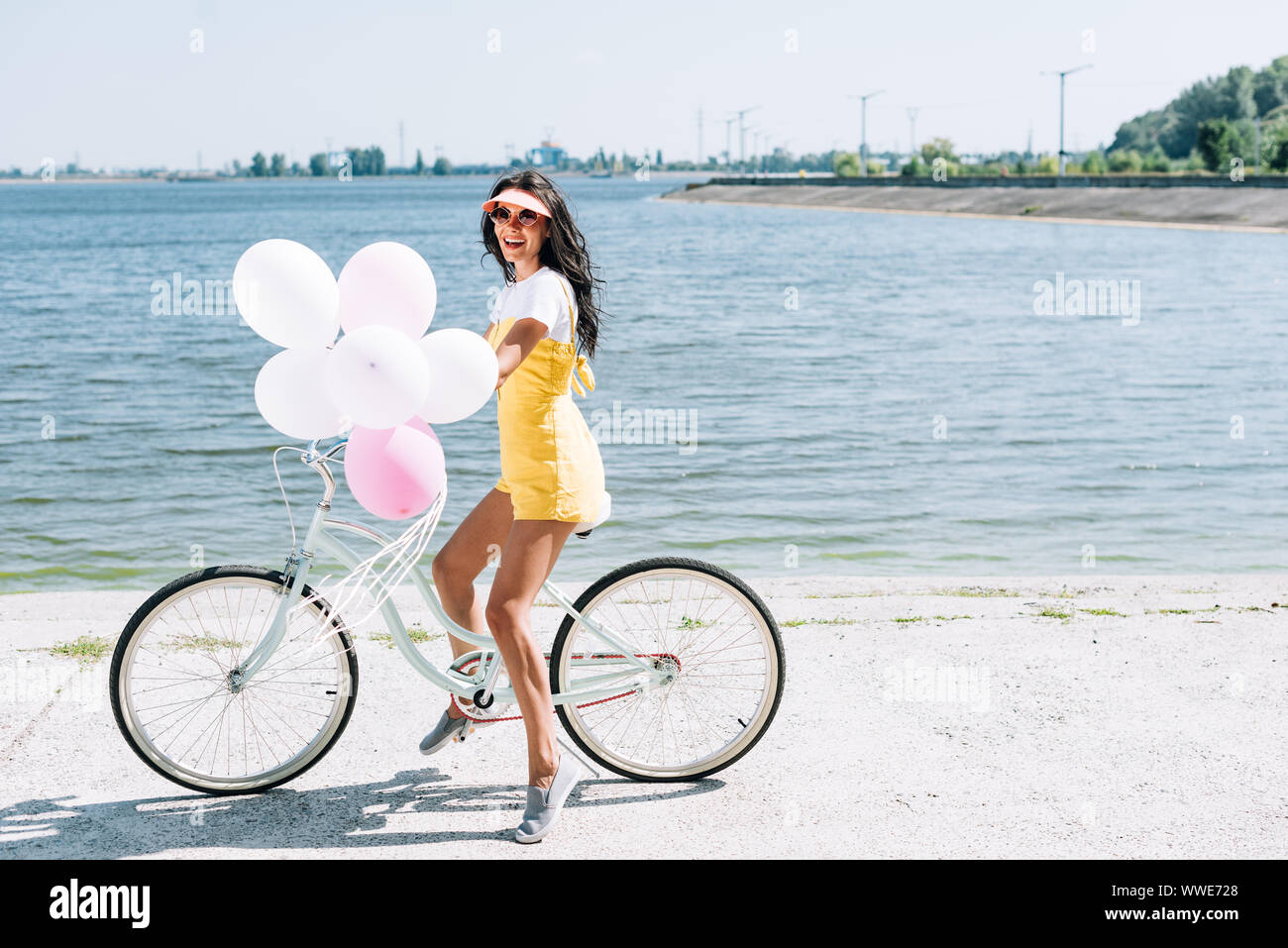 side view of beautiful brunette girl riding bike with balloons near river Stock Photo - Alamy