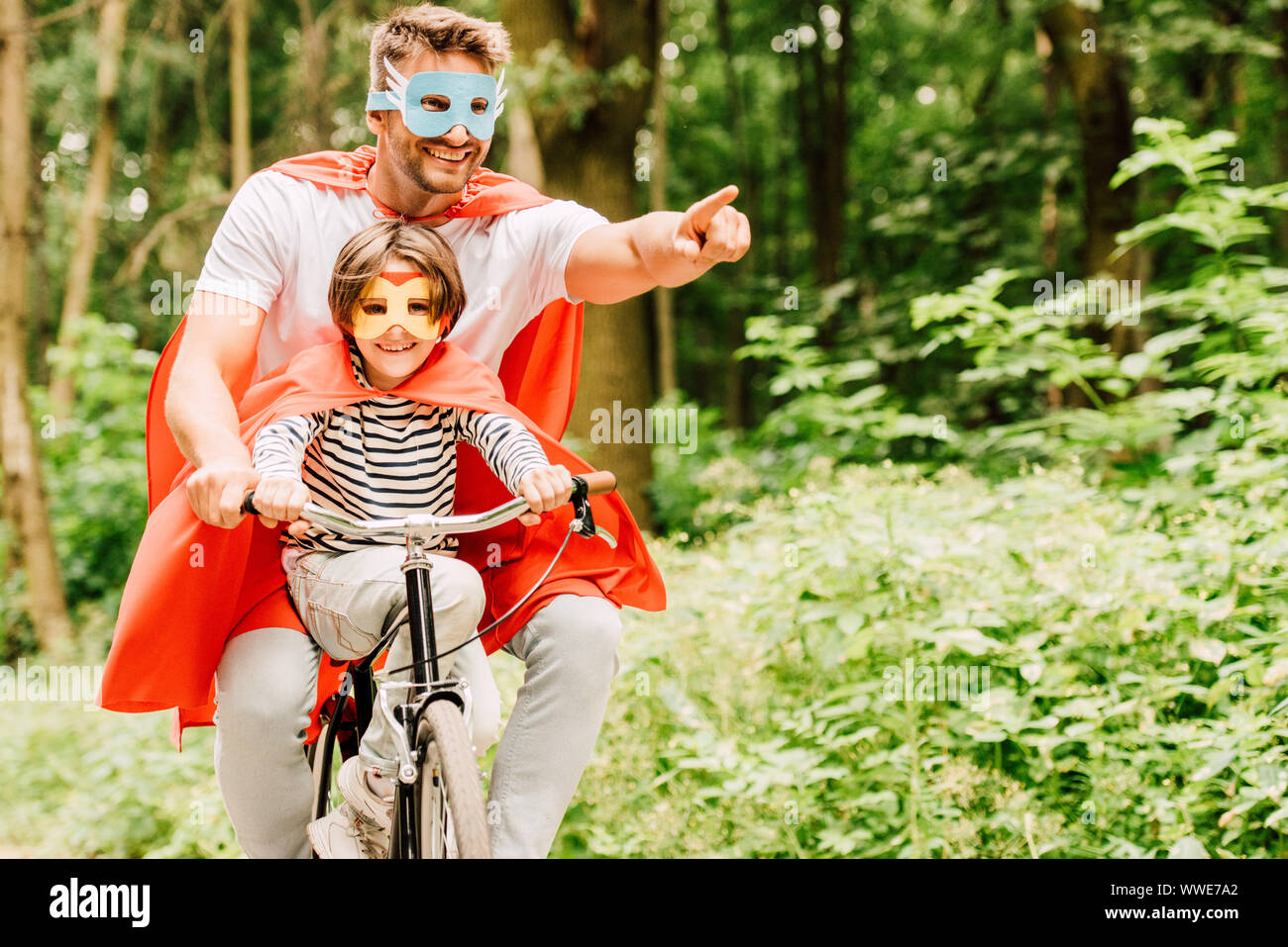 father and kid riding bicycle around forest in superhero costumes Stock ...