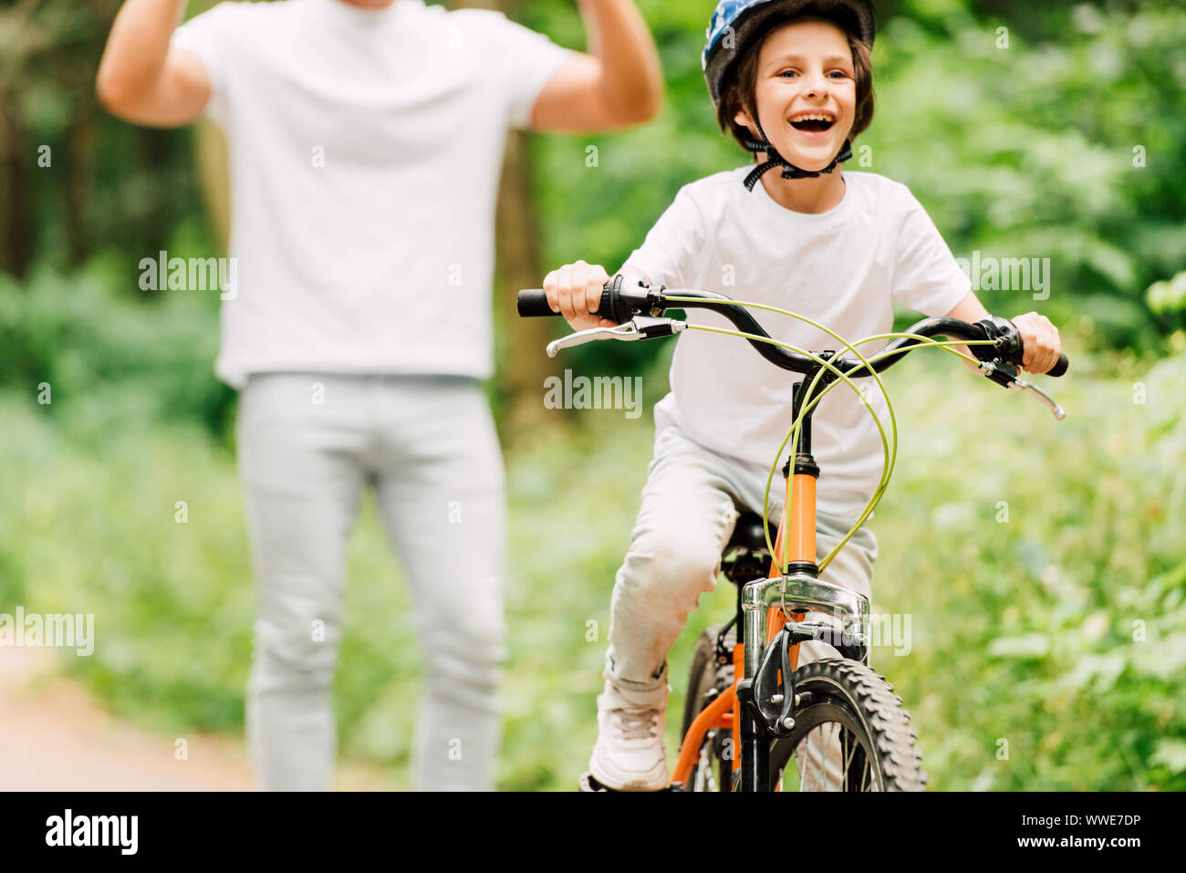 cropped view of cheering son while boy riding bicycle and looking away ...