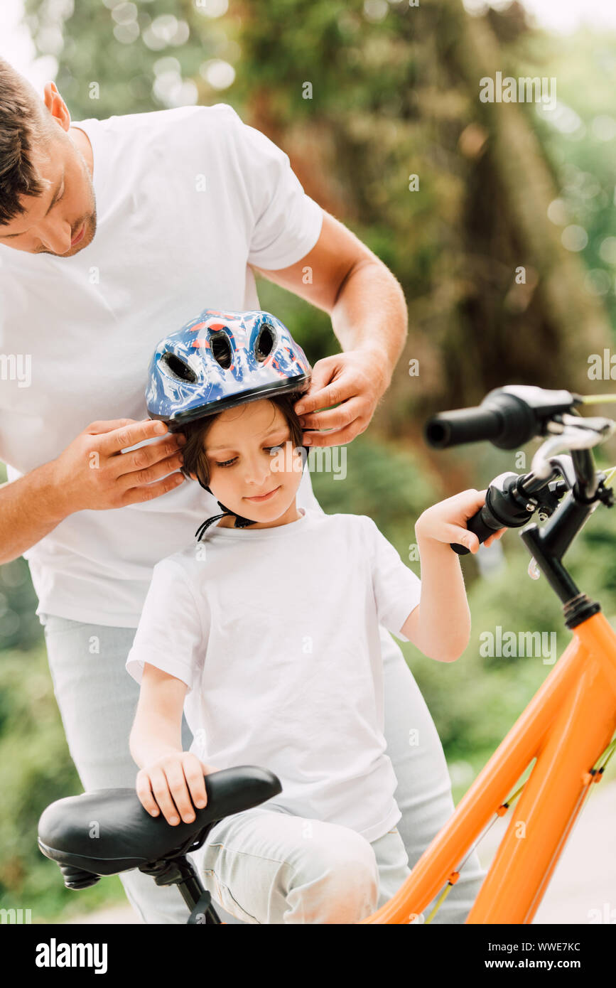 father putting helmet on son while boy trying to sit on bicycle Stock ...
