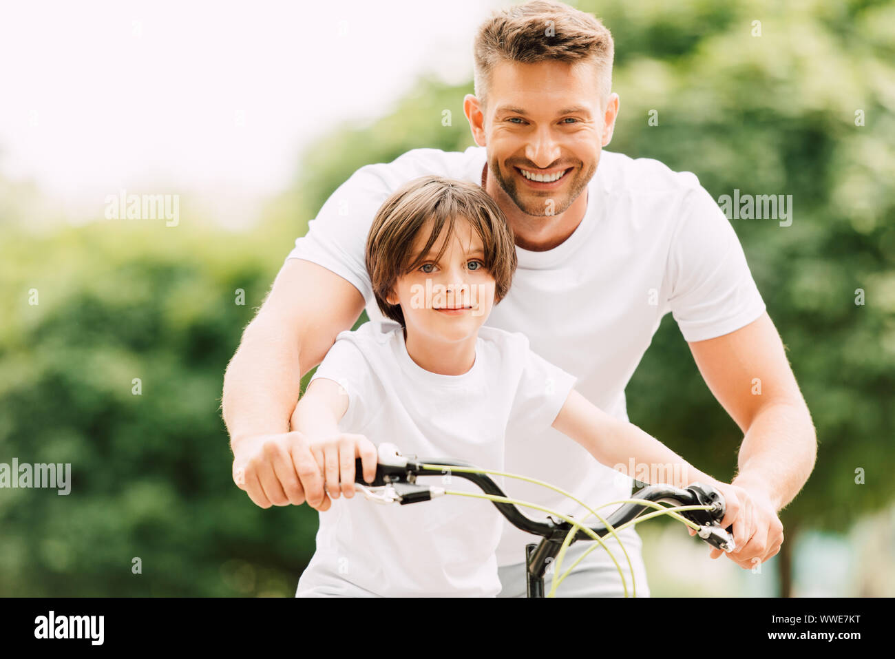 happy father and son looking at camera while boy siting on bicycle dad ...